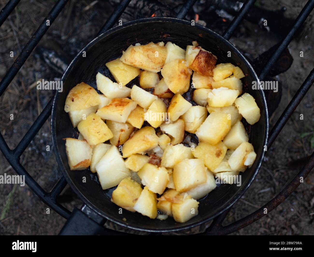 Potatoes are fried in a pan mounted on a wire rack over a fire Stock ...