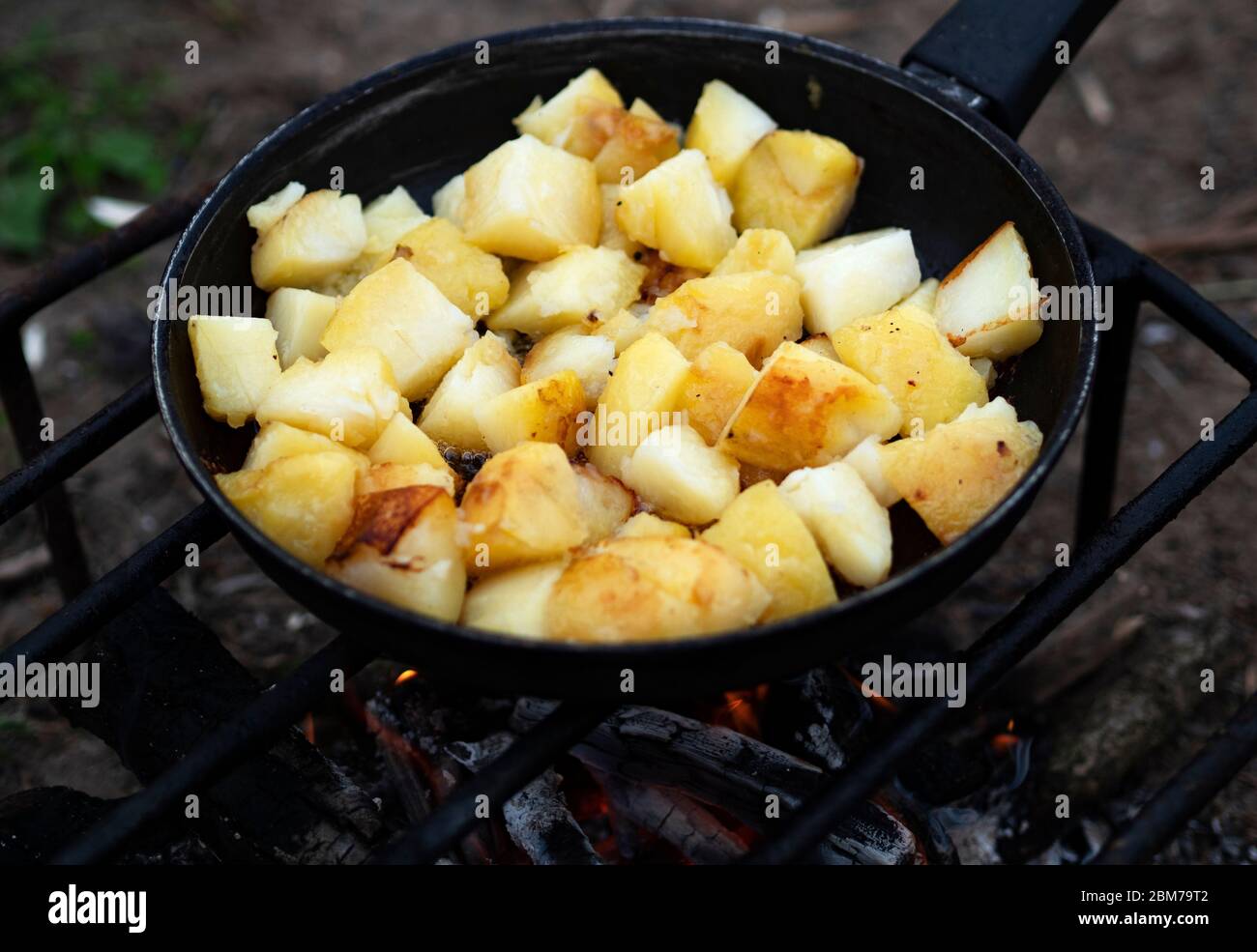 Potatoes are fried in a pan mounted on a wire rack over a fire Stock ...
