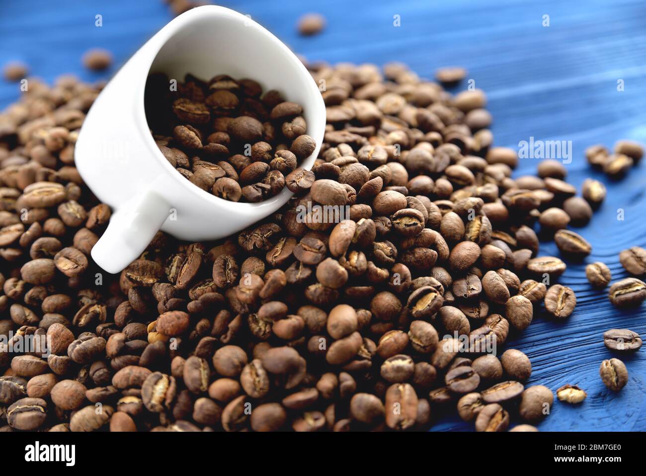 white cup in coffee beans lying on a blue wooden background, close-up ...