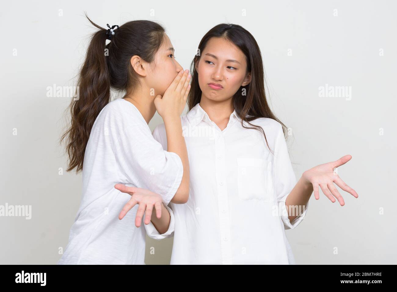 Two young beautiful Asian women as friends whispering to each other ...
