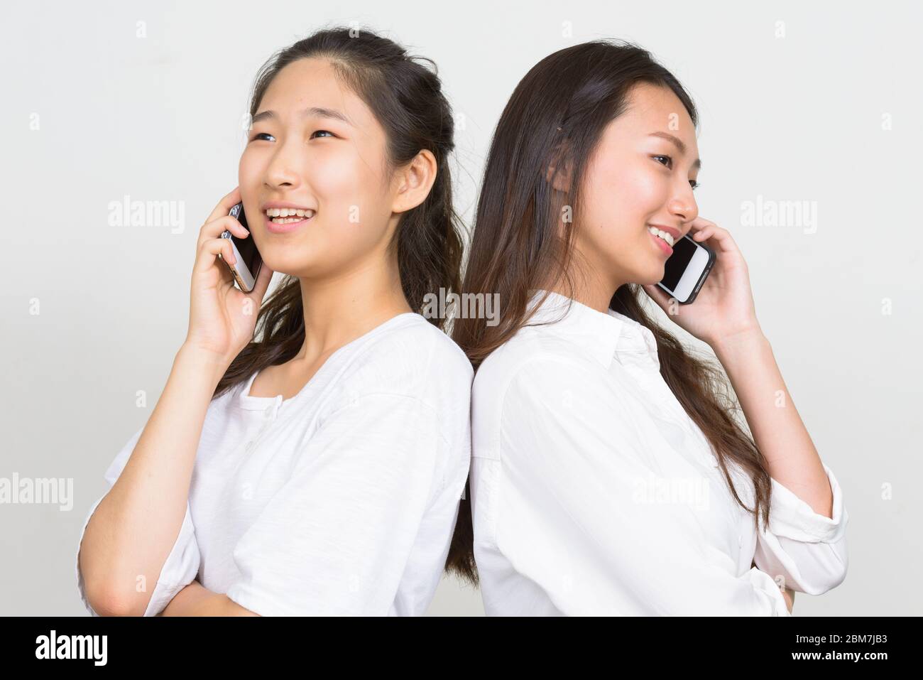 Two happy young beautiful Asian women as friends talking on the phone ...