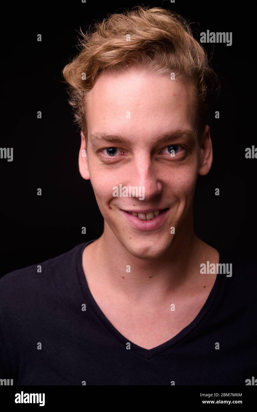 Face of happy young blond Scandinavian man smiling against black ...