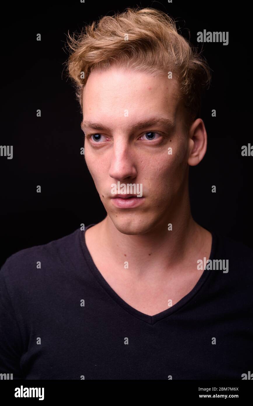 Face of young blond Scandinavian man thinking against black background ...