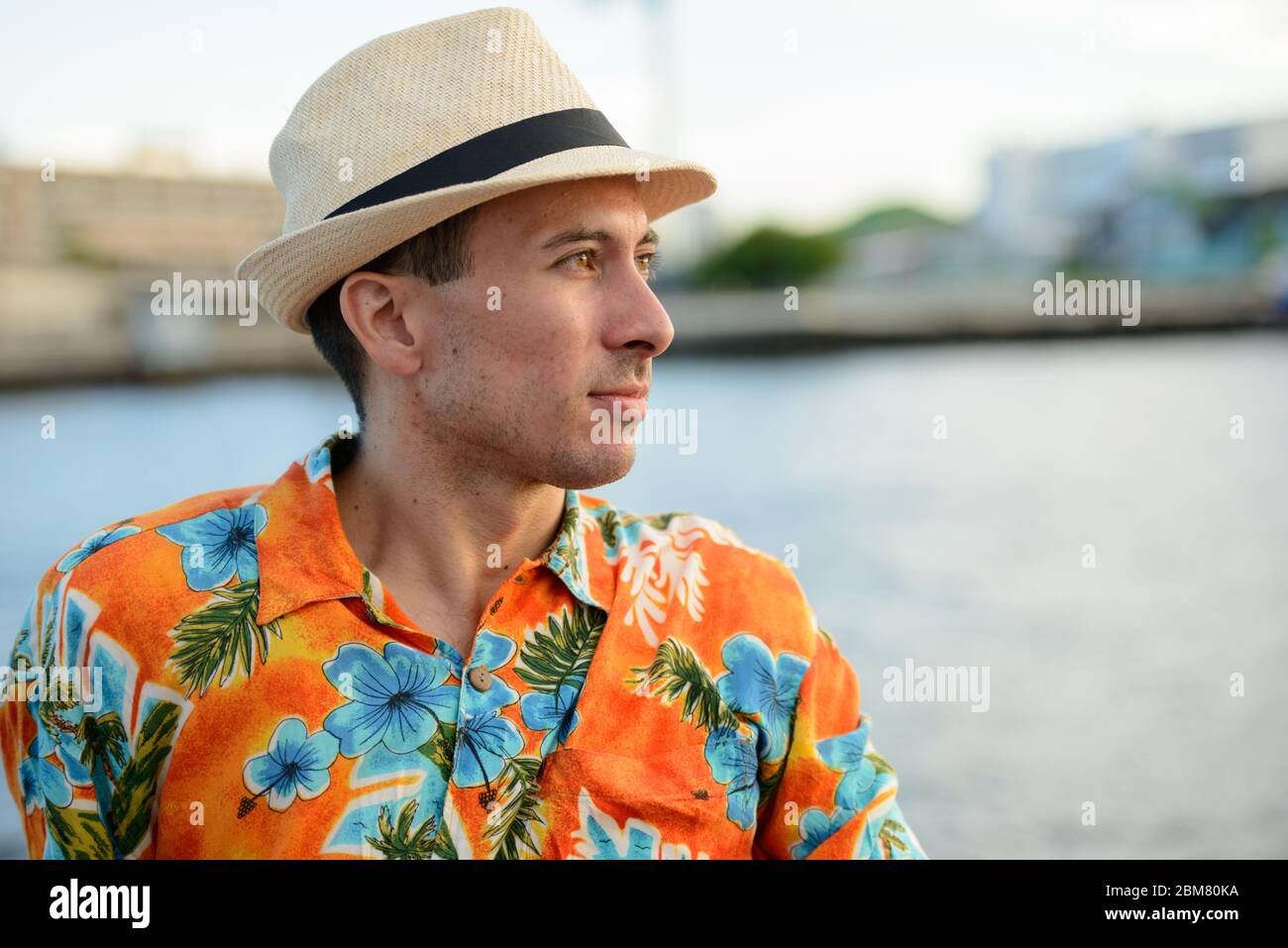 Young handsome tourist man thinking at pier against view of the river ...