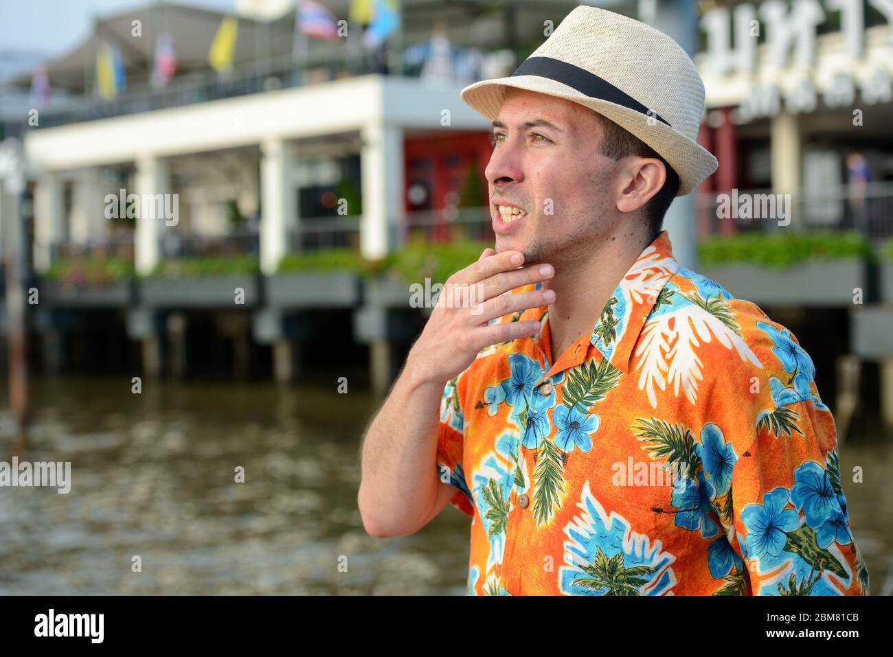 Young handsome tourist man thinking at pier against view of the river ...