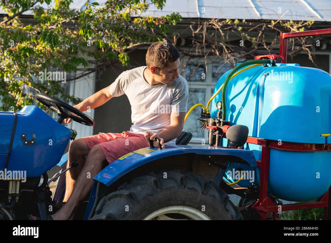 Casual man sitting on a tractor with sprayer, looking at the back side ...