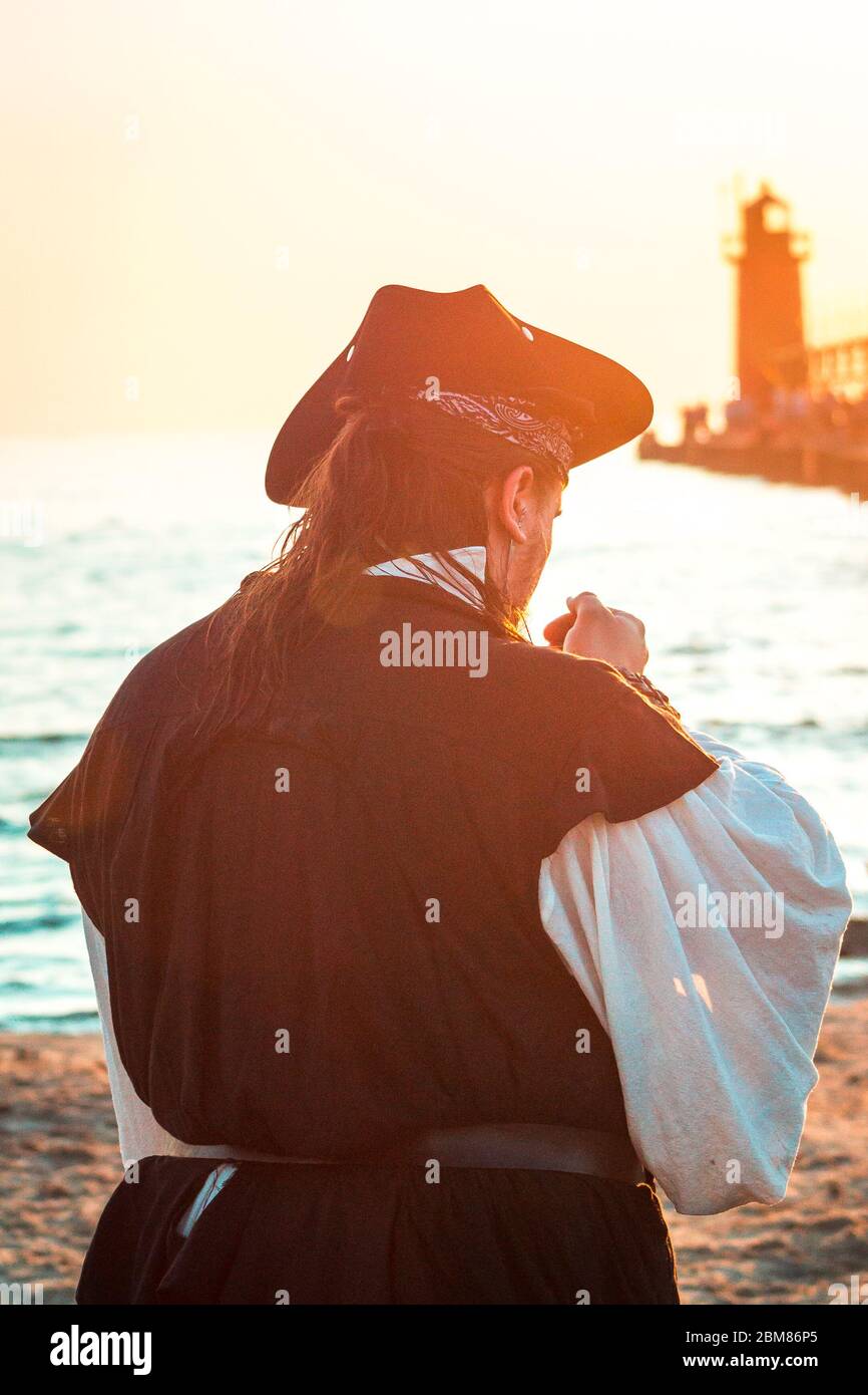Man dressed up as a pirate smoking a pipe at sunset by a lighthouse ...