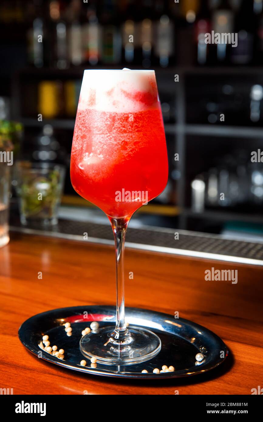 Sweet cold cocktail of red color stands on a wooden table in a pub ...