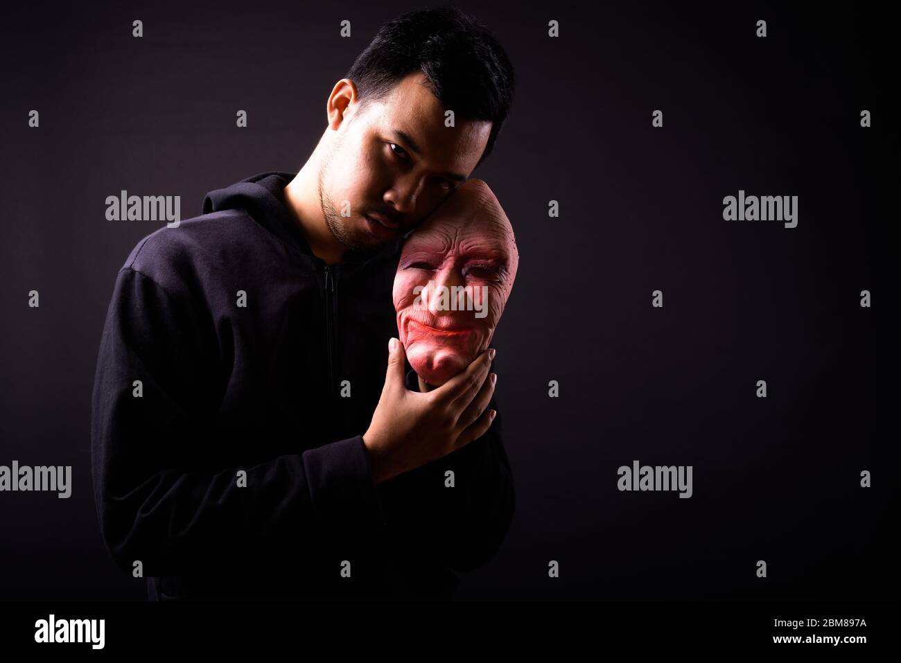 Portrait of crazy young Asian man with hoodie holding horror mask Stock ...