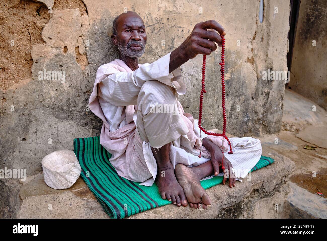 Muslim man sitting on the floor on a mat, praying with a rosary in his ...