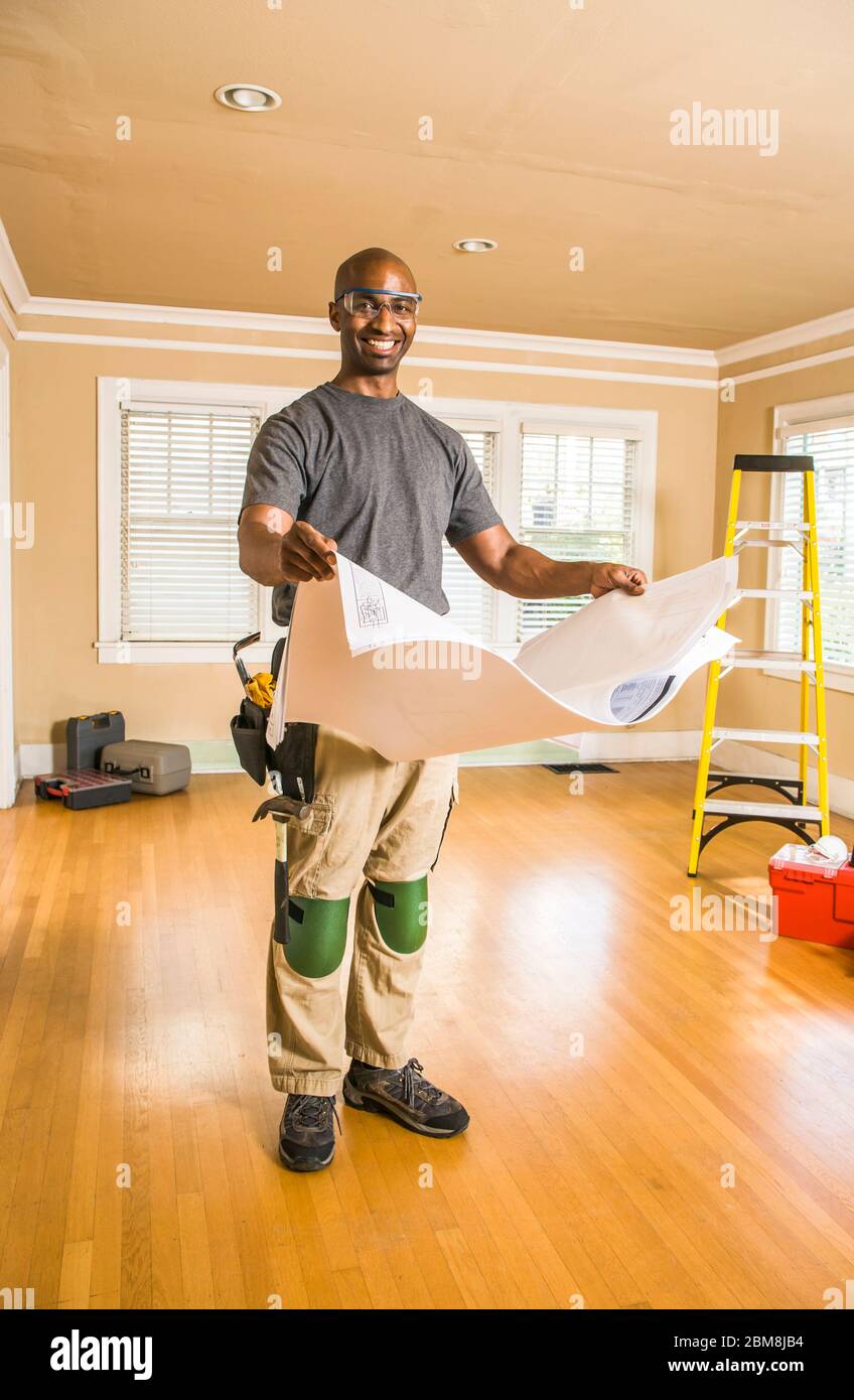 An African American man looking at building plans wearing a tool belt ...