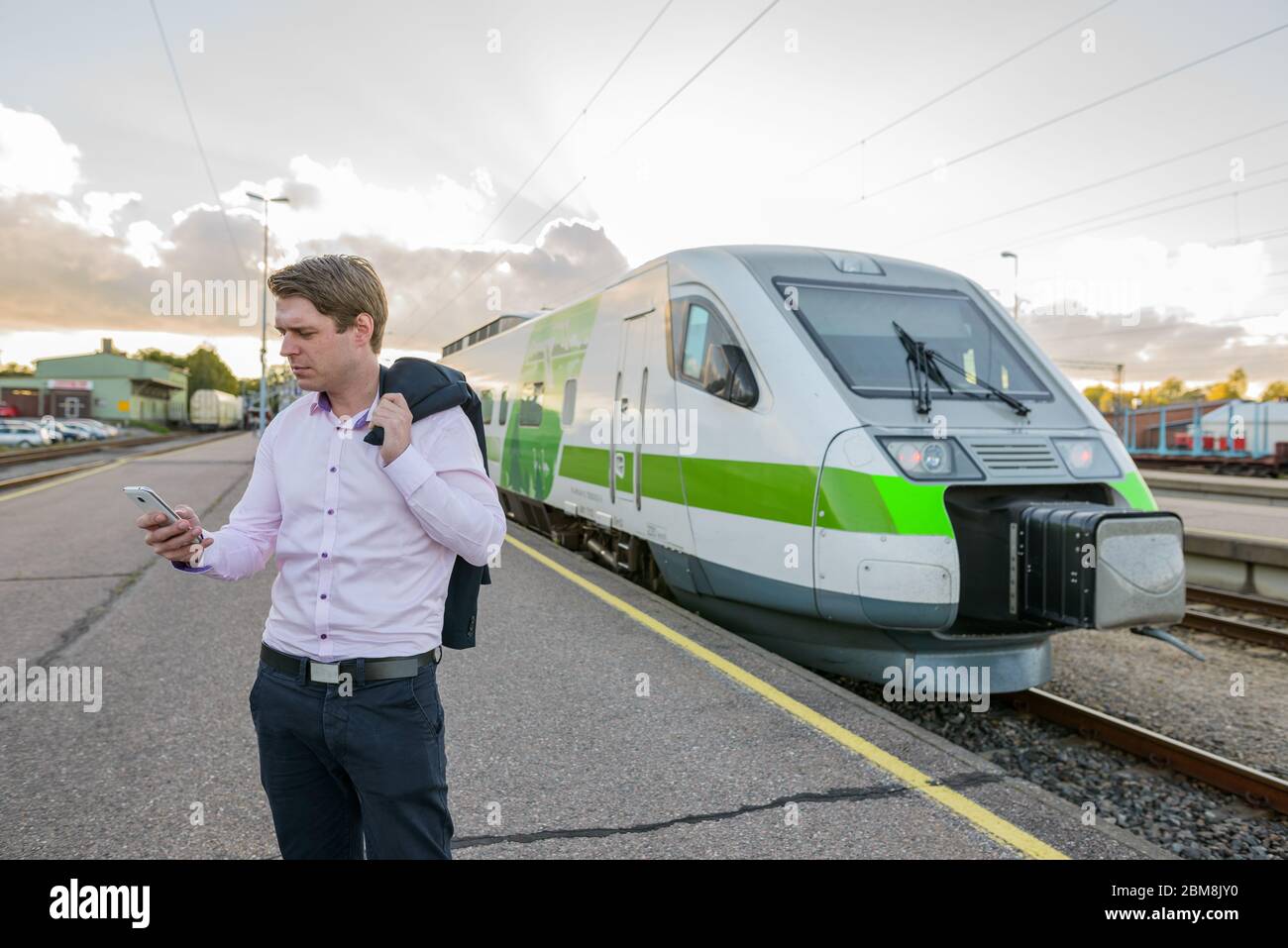 Young handsome businessman using mobile phone in front of train at ...