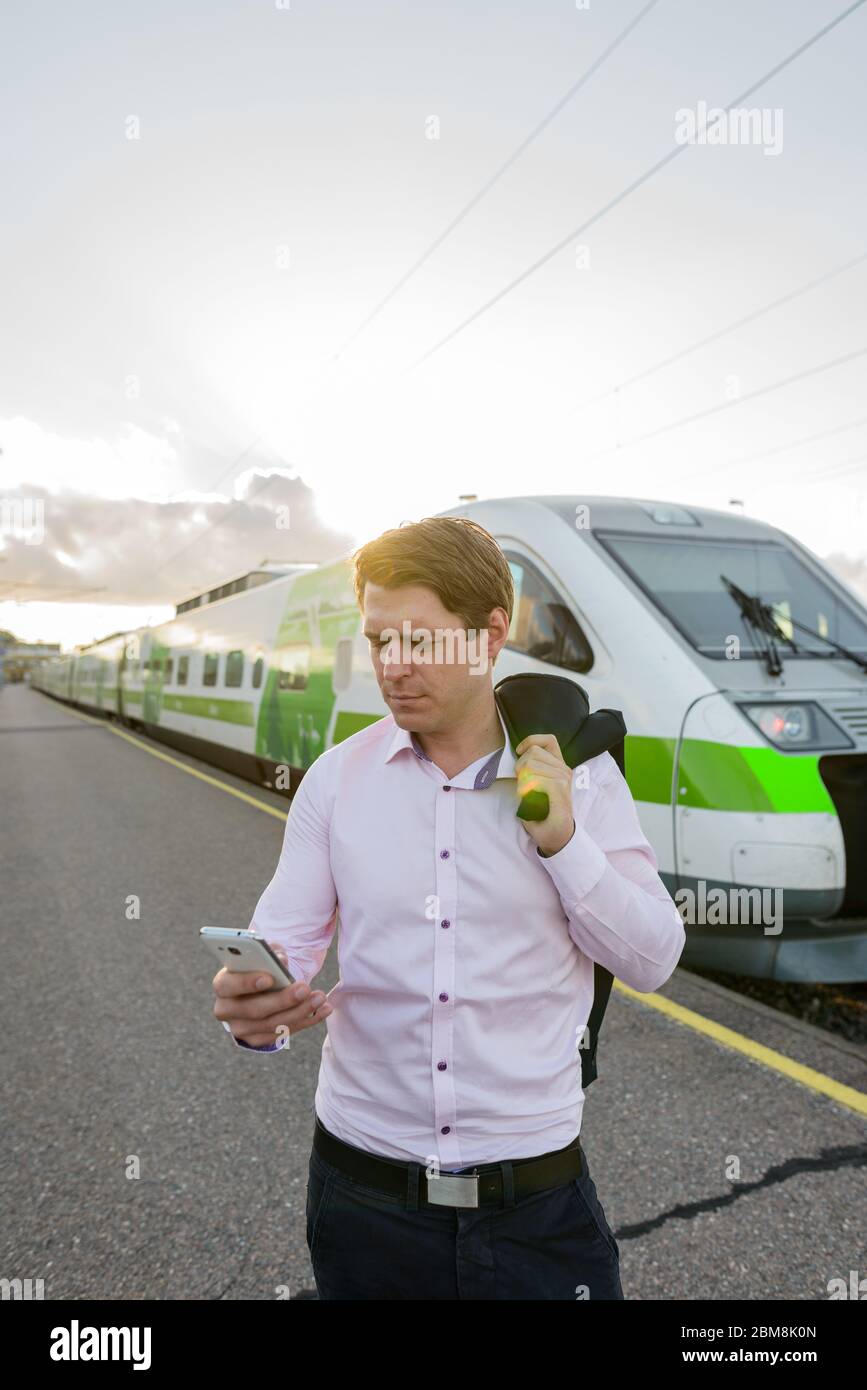 Young handsome businessman using mobile phone in front of train at ...