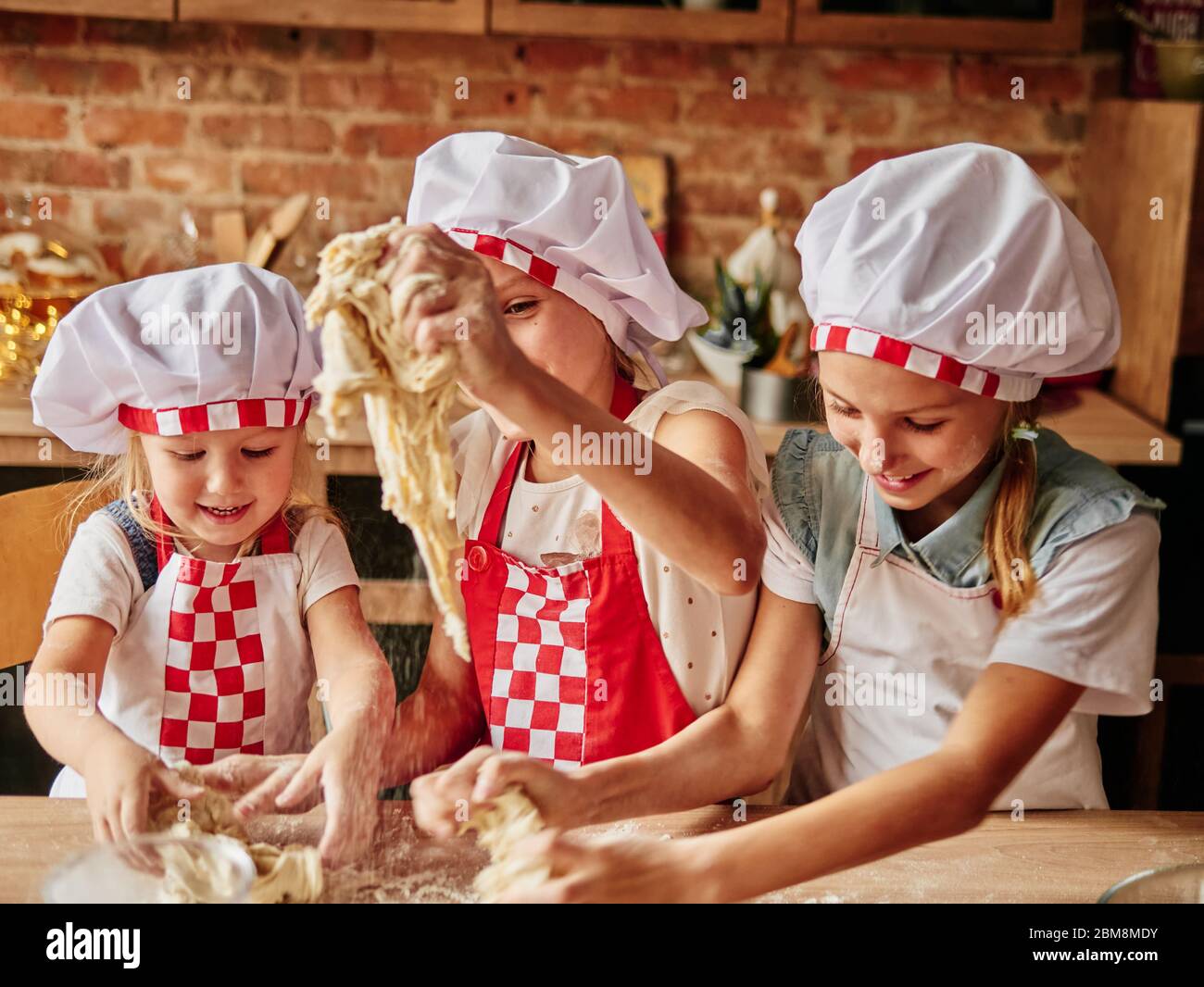 Three little chefs enjoying in the kitchen making cakes. Girls at the ...
