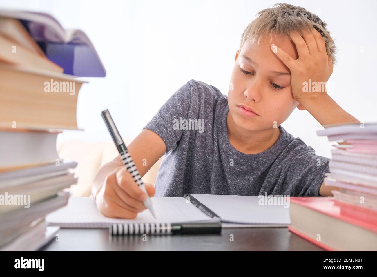 Schoolboy sitting among pile of books, textbooks, school exercise books ...