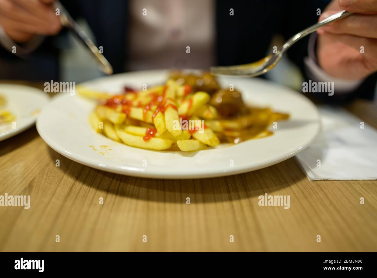 Hands of businessman eating french fries and meatballs at the ...