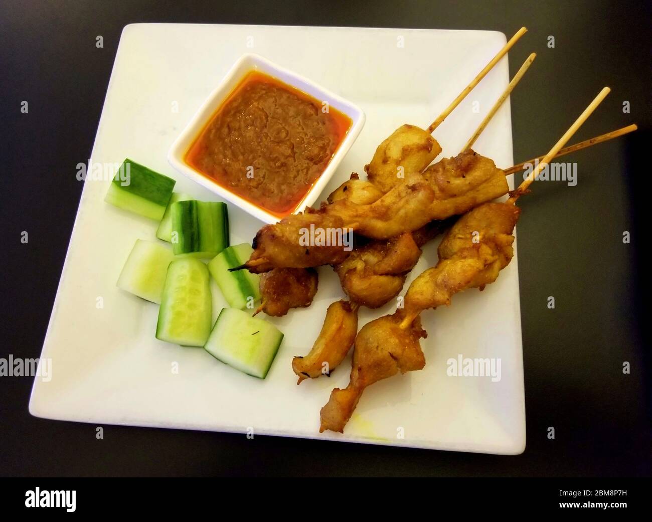 Malaysian chicken satay with peanut sauce and slices of cucumber on a ...