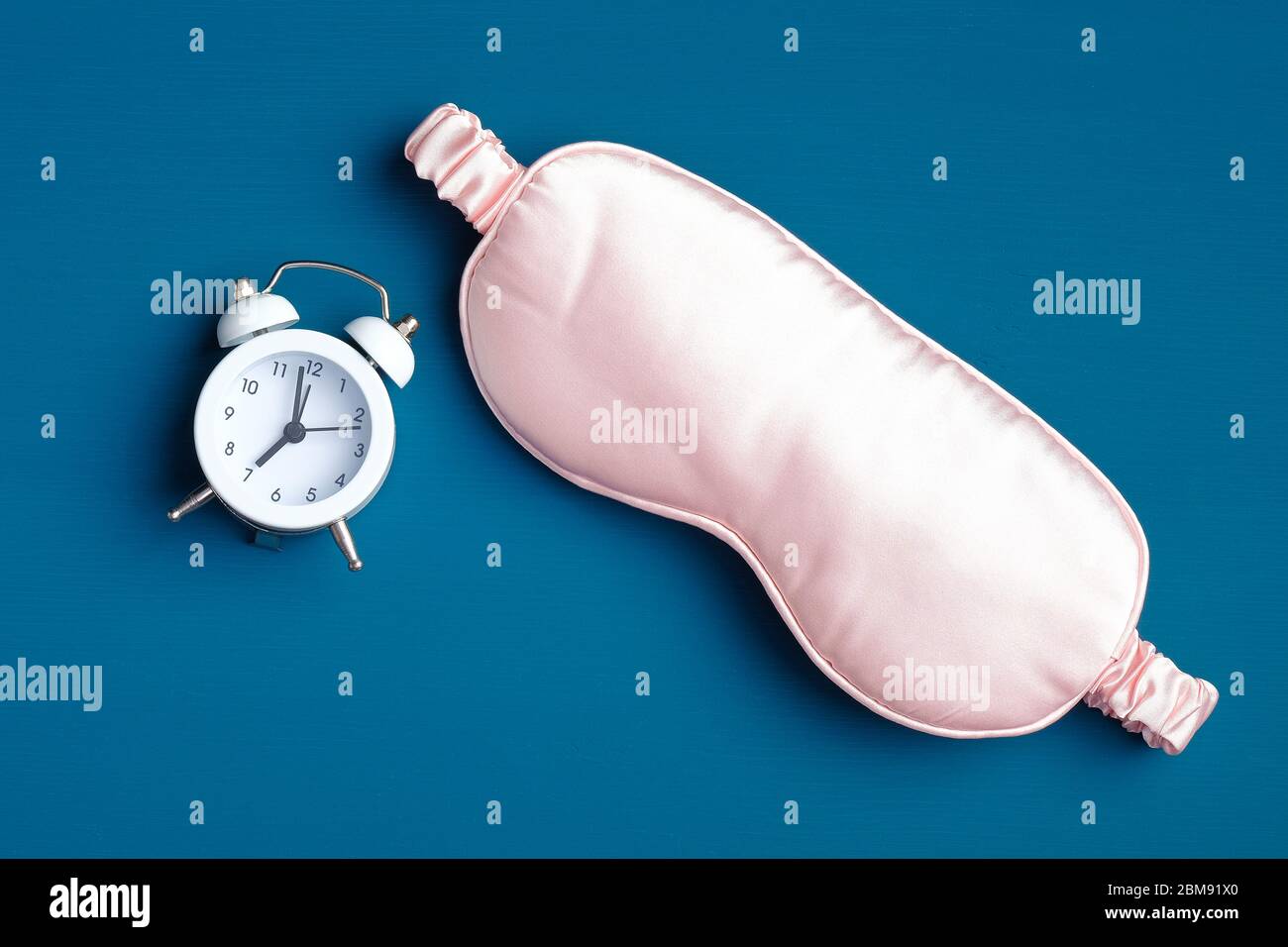 Pink sleep eye mask and white alarm clock on dark blue background ...