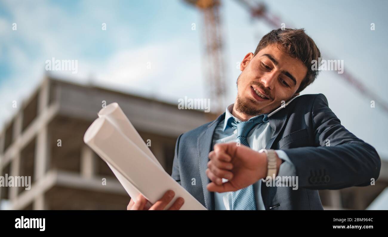 Young male construction engineer or businessman talking on phone looks ...