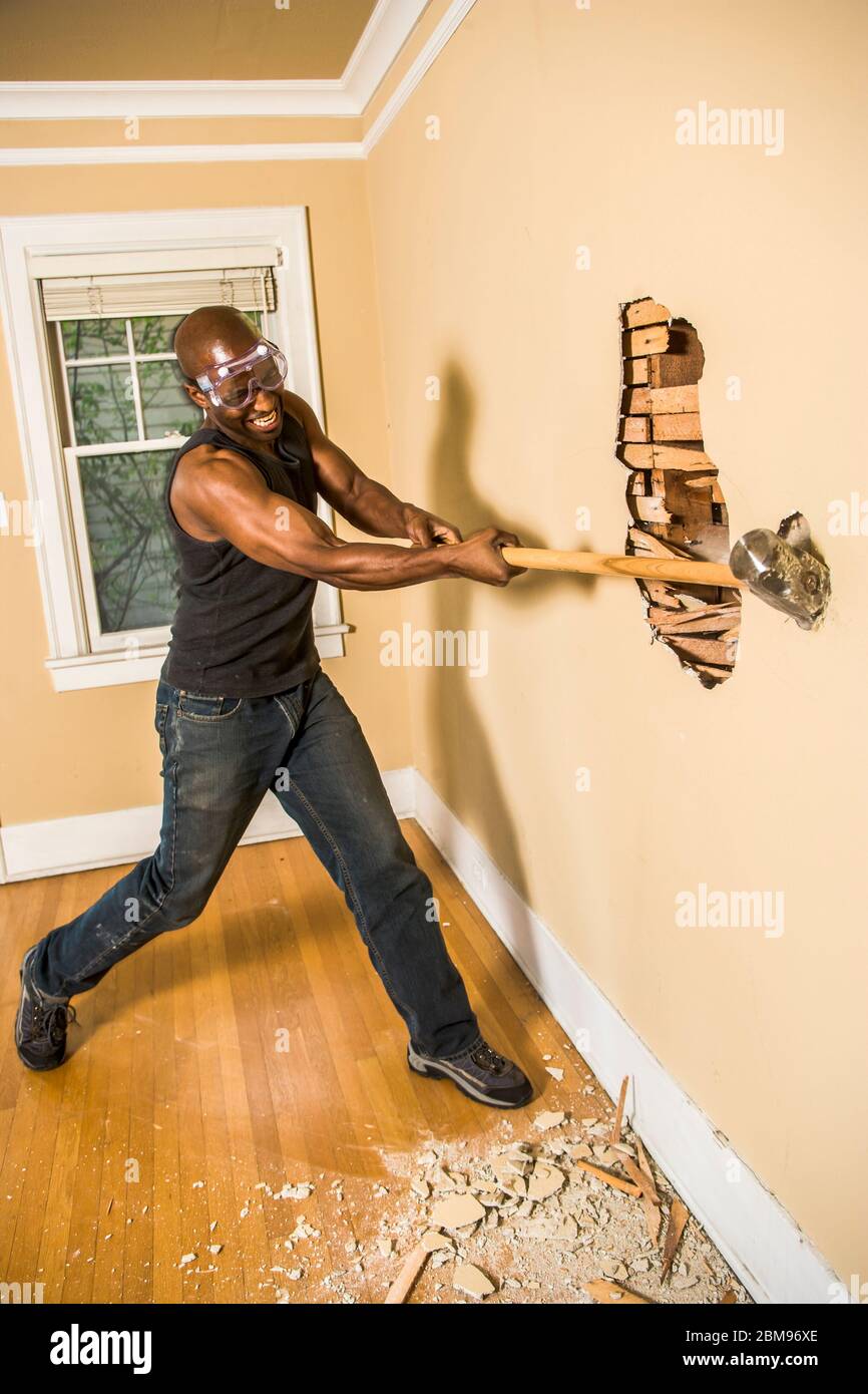 A man swings a sledgehammer at a interior wall of a home Stock Photo ...