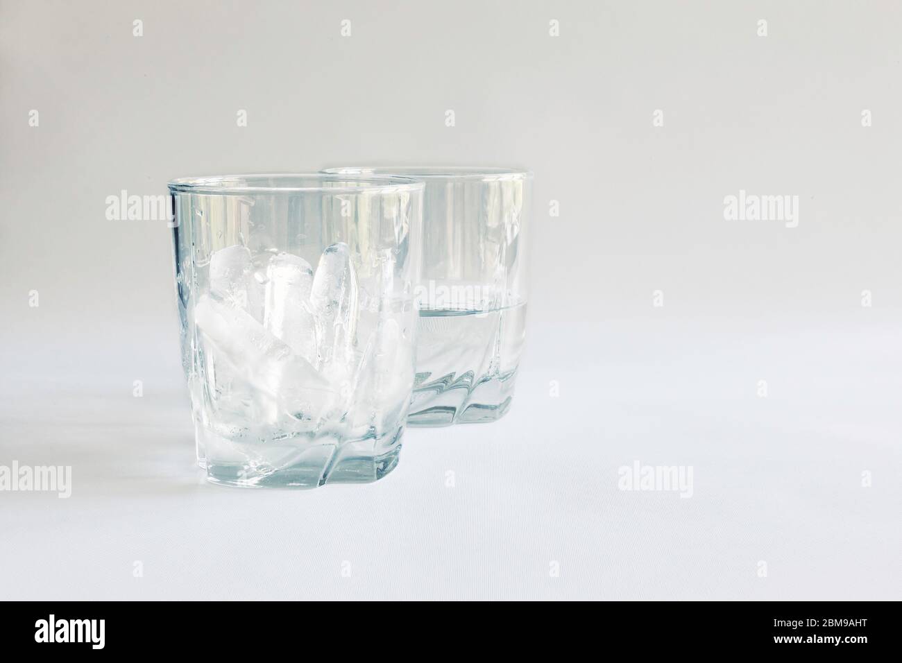 Tumbler full of ice with a second glass half full of water (ice melted ...