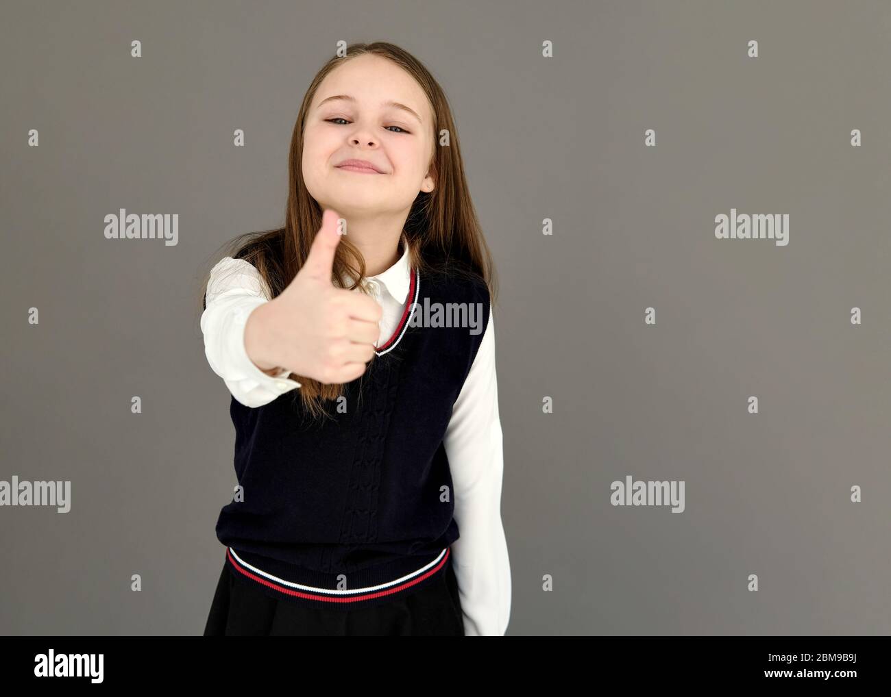 a beautiful school girl in school uniform smiles and shows a cool ...
