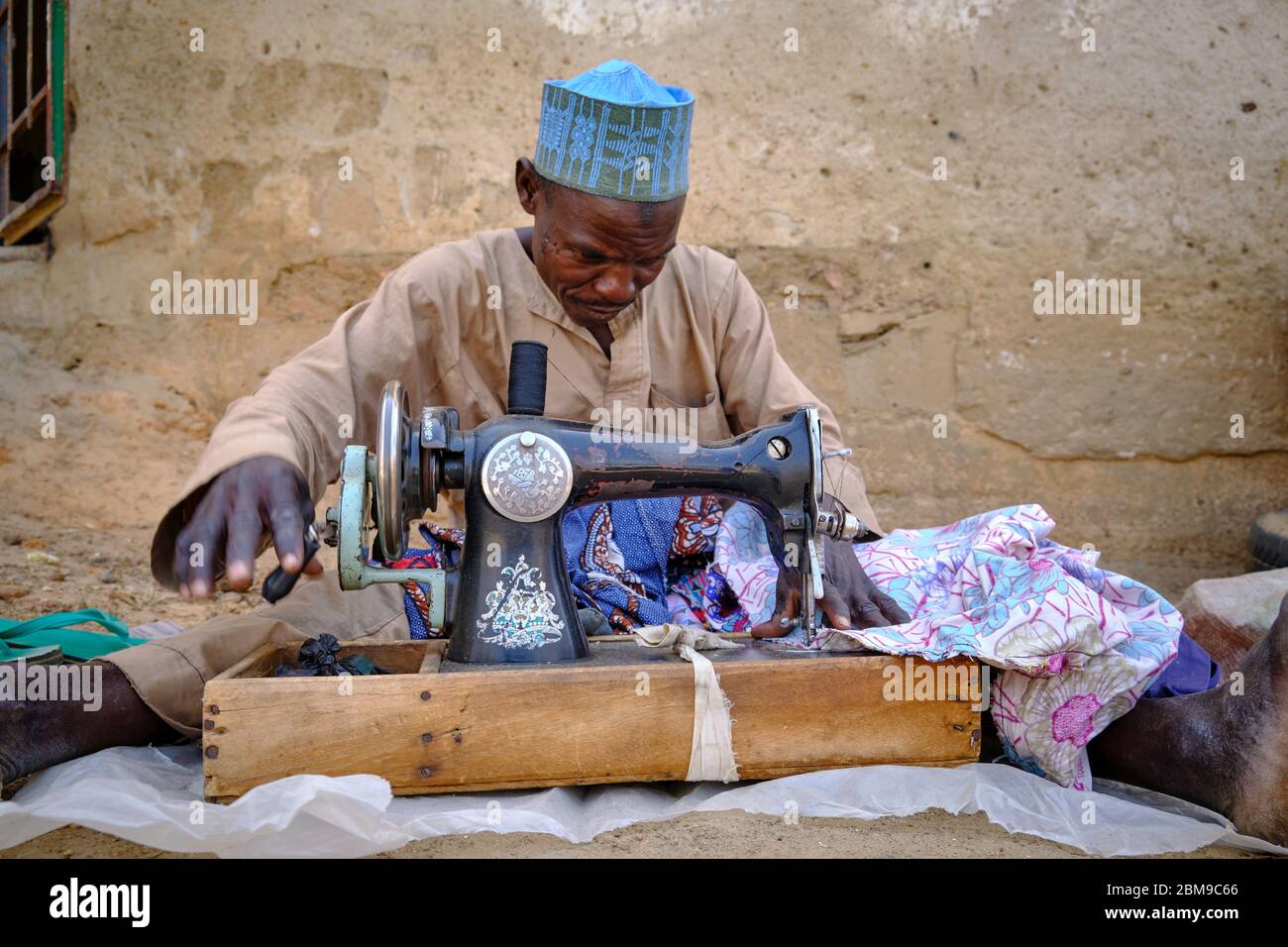 Tailor sitting on the floor sewing with an old machine at a market in ...