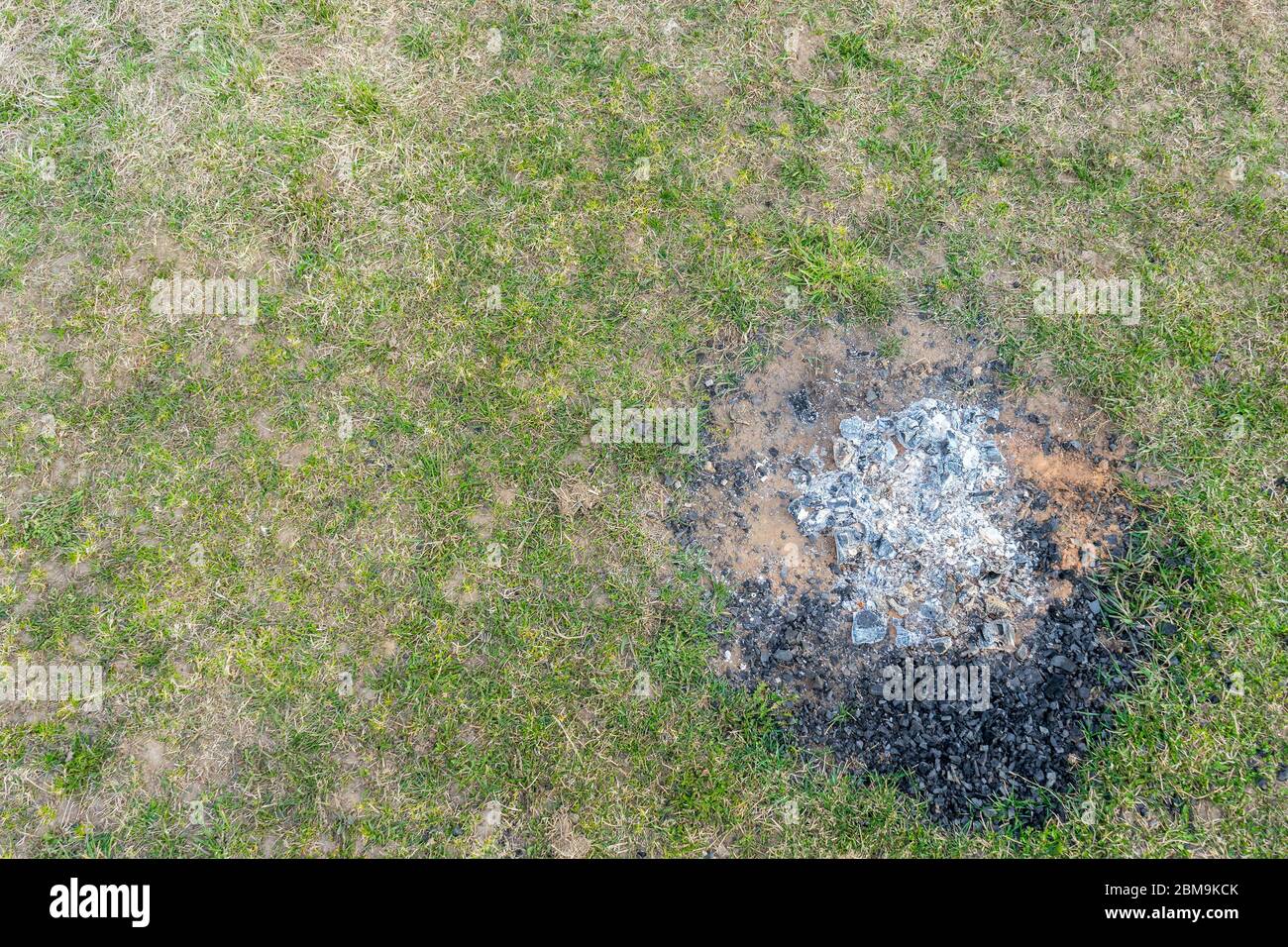 Remains of fire, ashes and cold coals on site of fire on ground covered ...