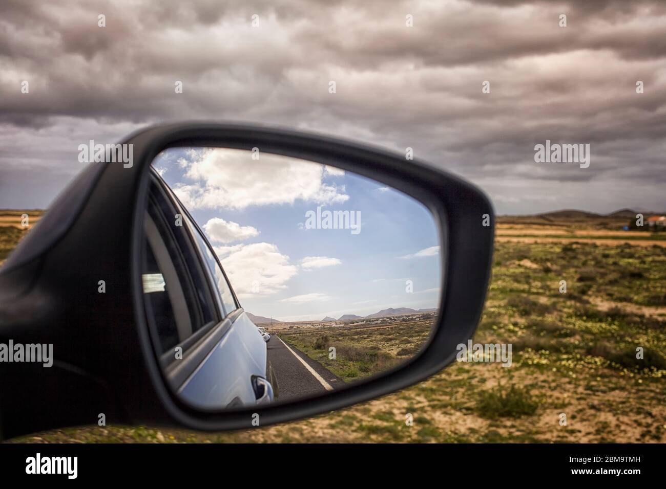 Dark clouds ahead and blue sky with white clouds in rear view mirror ...