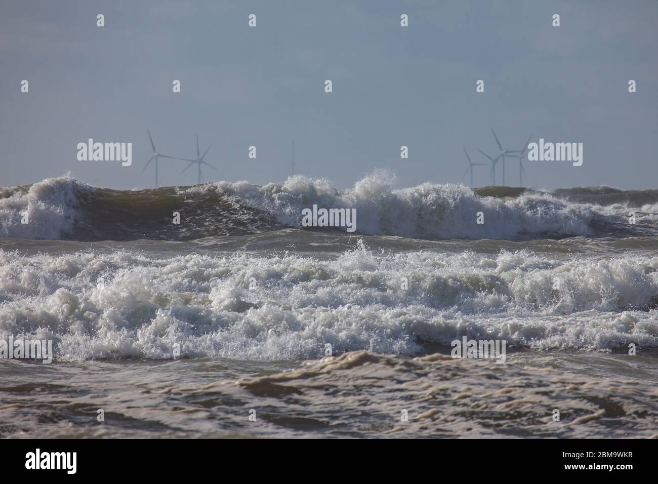 Waves of the north sea with white spindrift with wind wheels in the ...