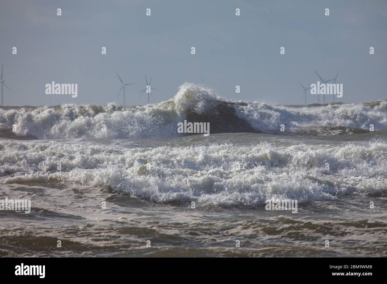 Waves of the north sea with white spindrift with wind wheels in the ...