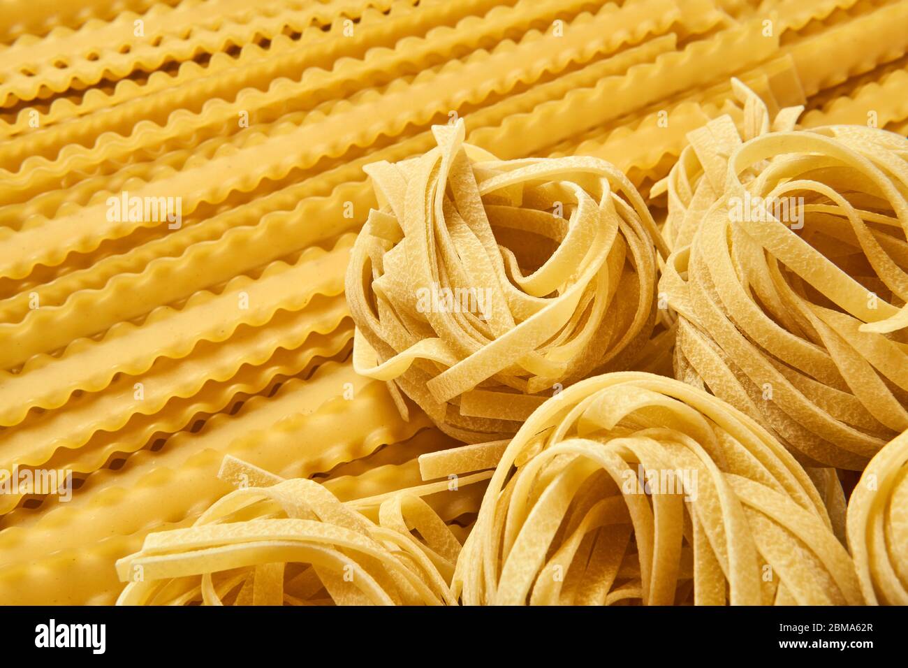 dry pasta tagliatelle and mafaldini warm background Stock Photo - Alamy