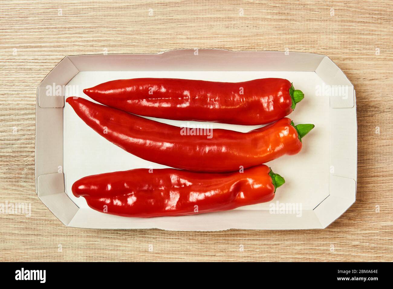 three pods of sweet red pepper lie in a cardboard tray on the table ...