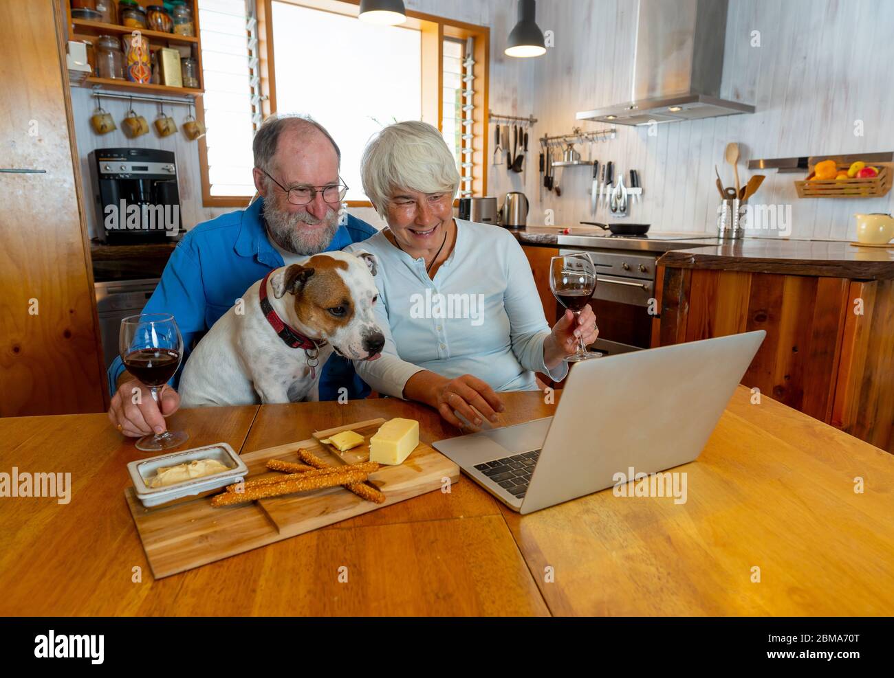 COVID-19 Stay connected. Happy senior couple with pet dog and wine ...