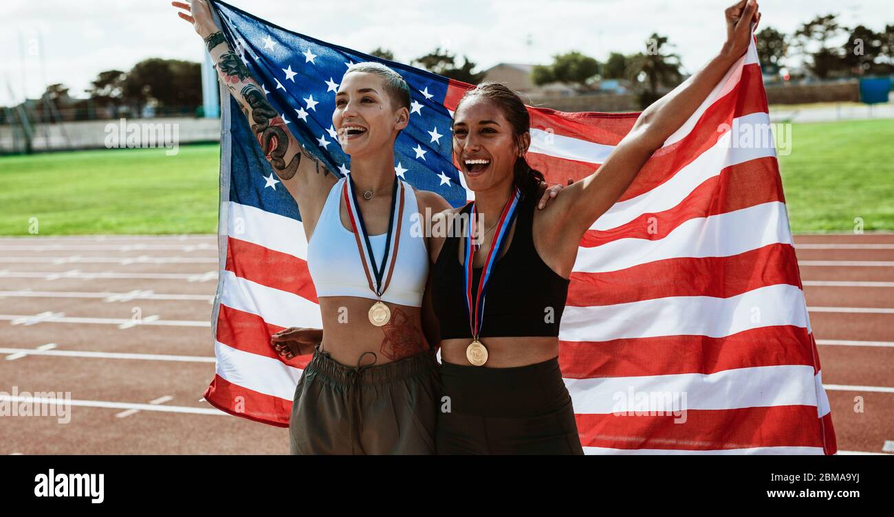 Female athletes on running track celebrating victory holding american ...