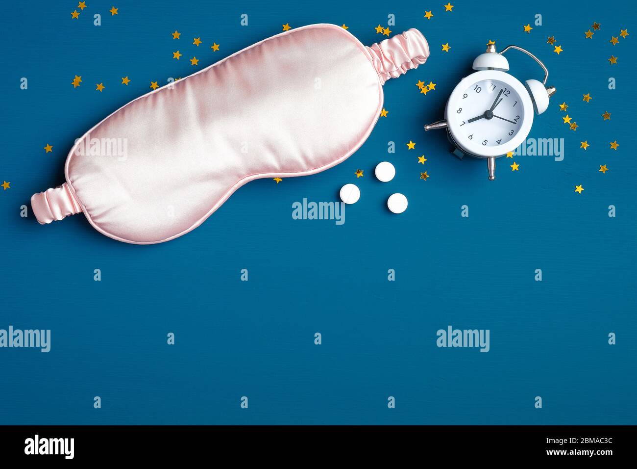 Pink sleep eye mask, alarm clock, sleeping aid on dark blue background ...
