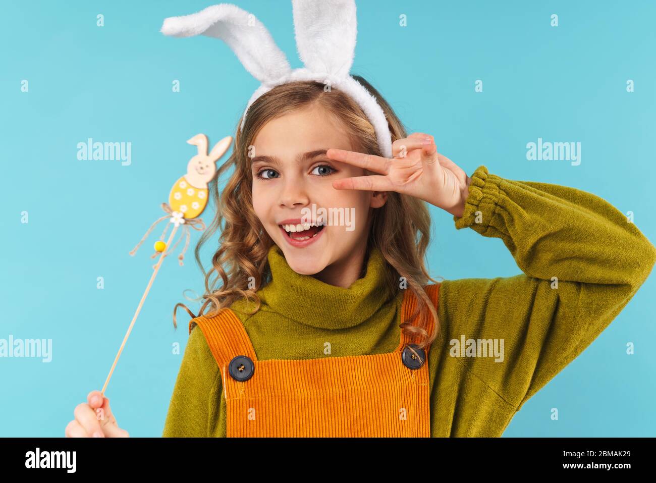 Photo of joyful curly girl in toy rabbit ears holding toy bunny and ...