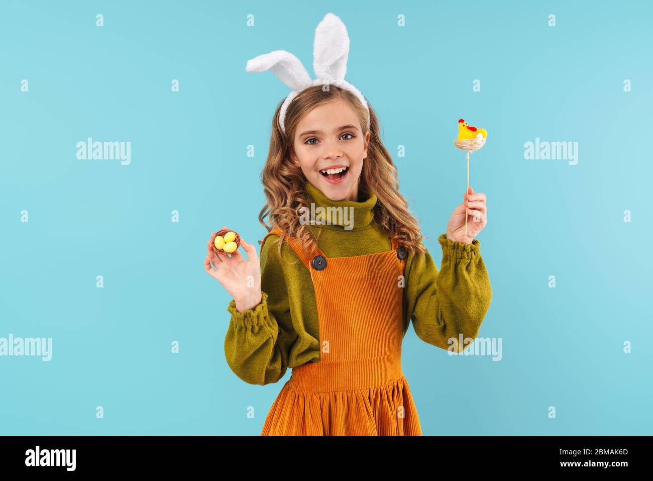 Photo of joyful blonde girl in fake rabbit ears holding colorful eggs ...