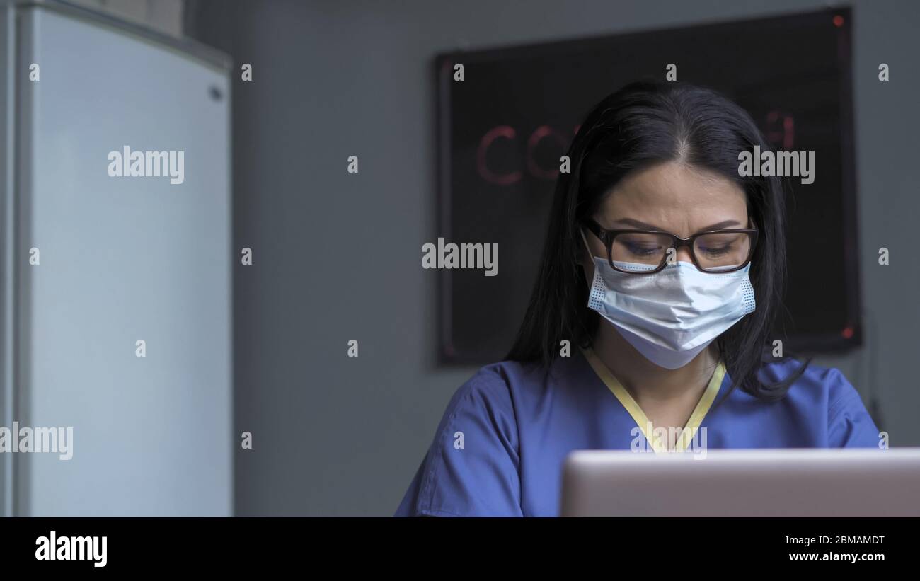 Tired female doctor works on computer sitting at desk in her office ...