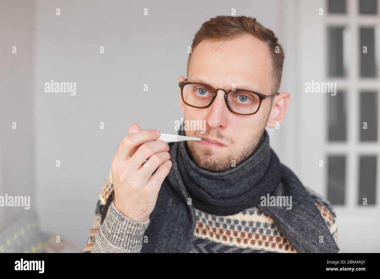 Sick man checking his temperature at home in the living room. Man in ...