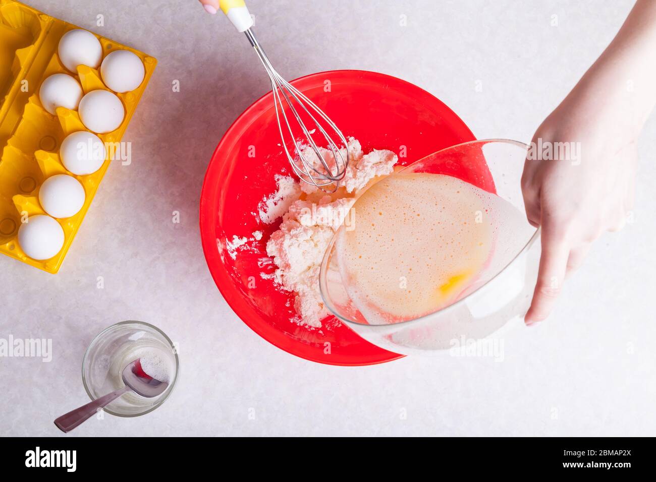 Female hands hold a whisk in one hand and with other pour whipped eggs ...