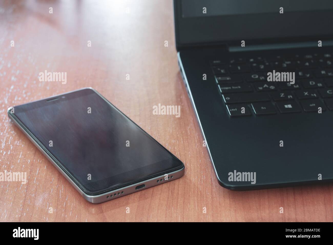 Black laptop and cell phone on the table. Selective shallow focus on ...