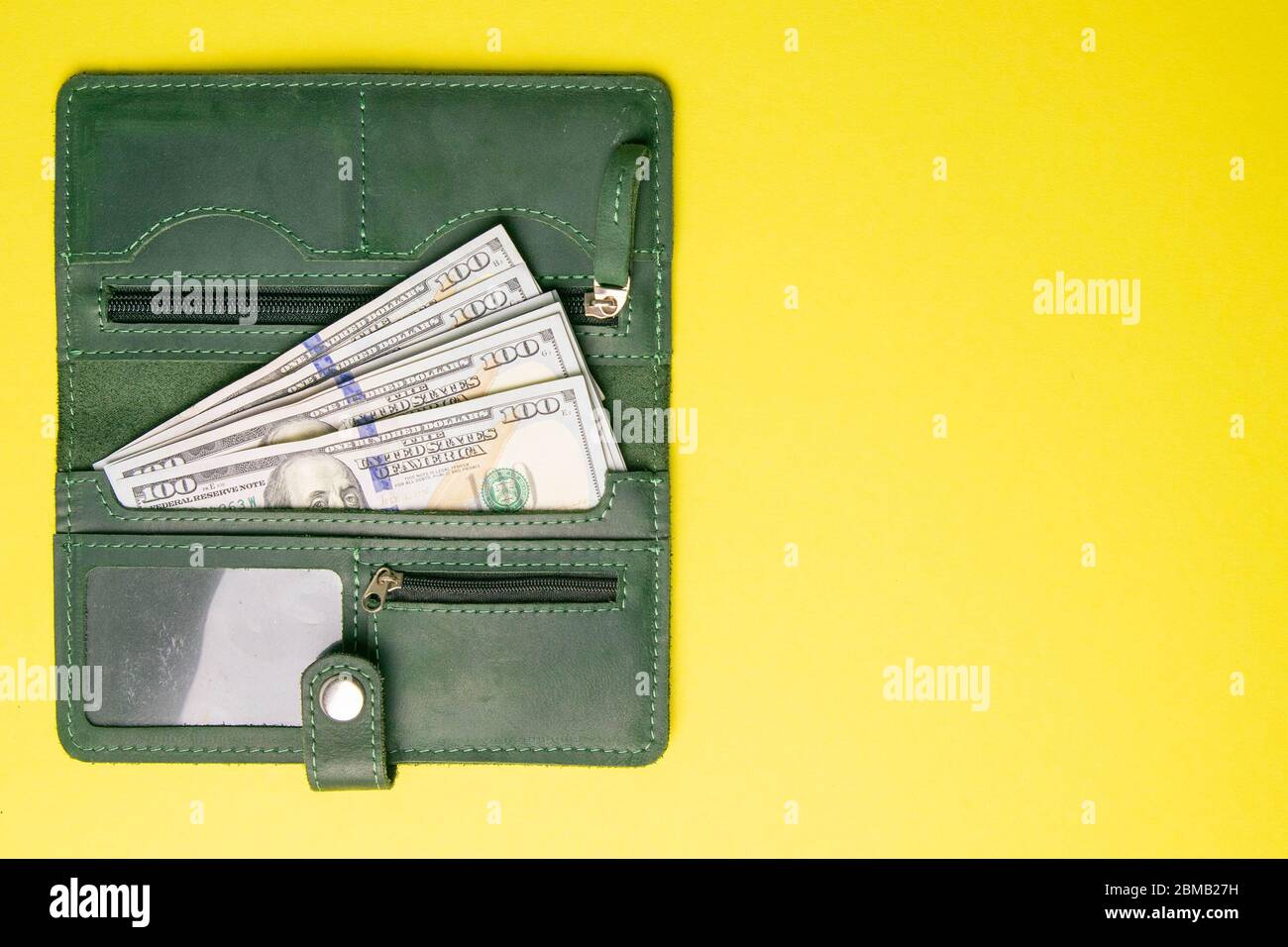Several hundred dollar bills protrude from a stylish green leather ...