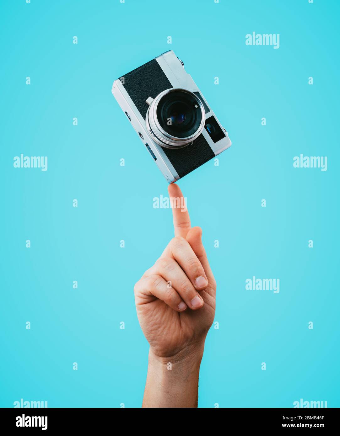 A vintage camera balanced over a finger on a man's hand, against a ...