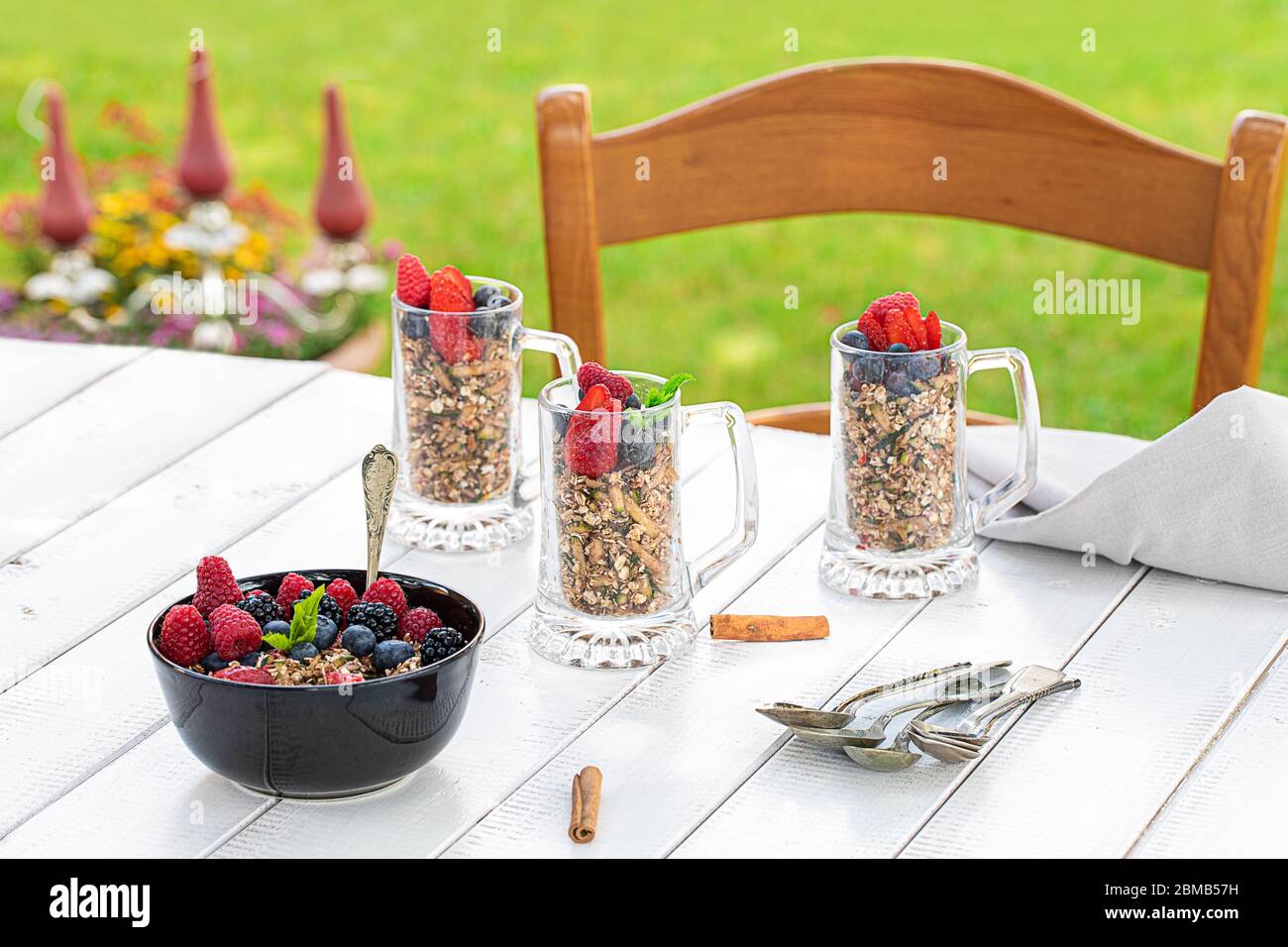 Outdoor breakfast with cereals and berries on white table and green ...