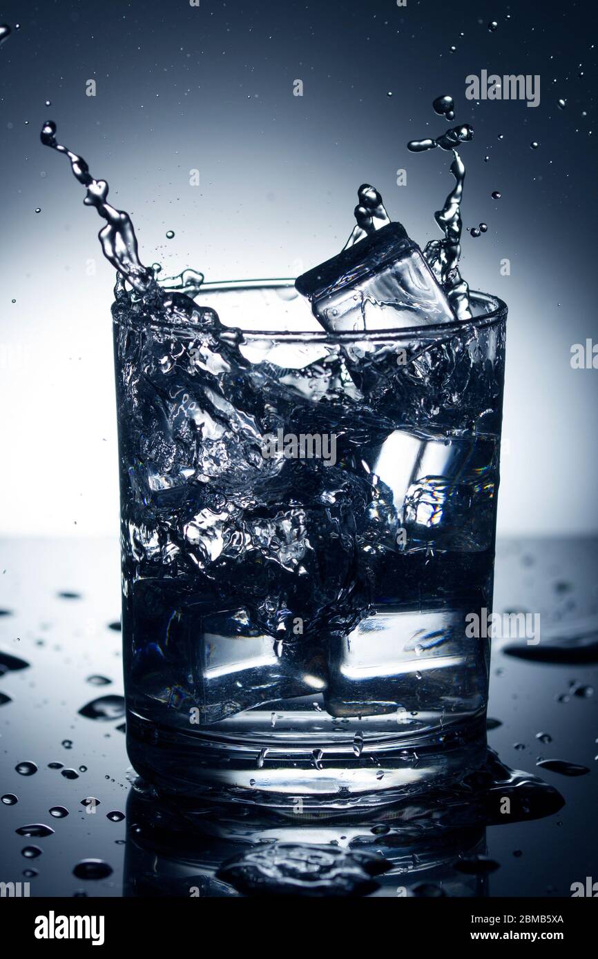 Glass of water with splash and ice on blue background Stock Photo - Alamy