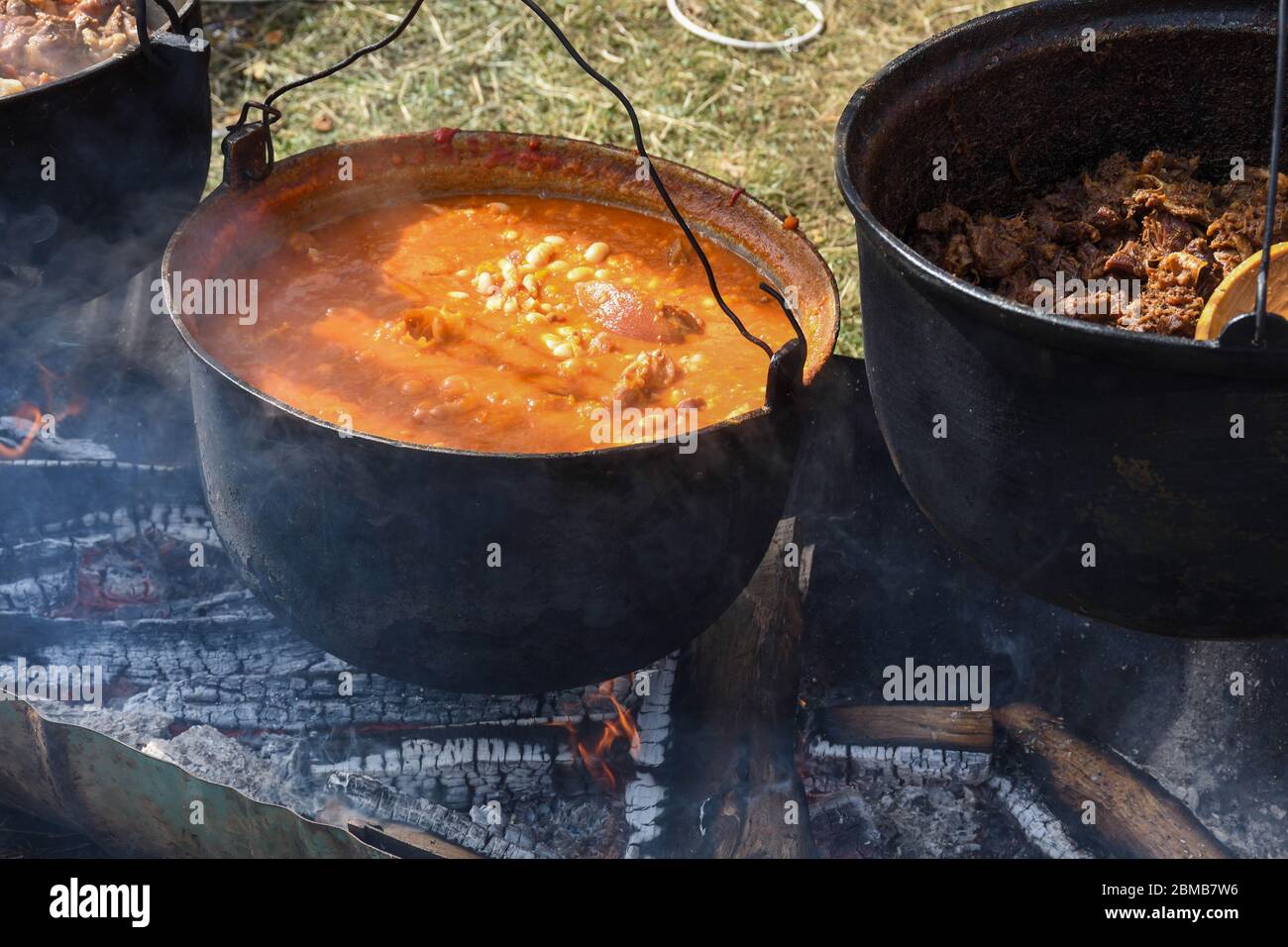 Very large cauldron cooking food during campfire, big pots on fire ...