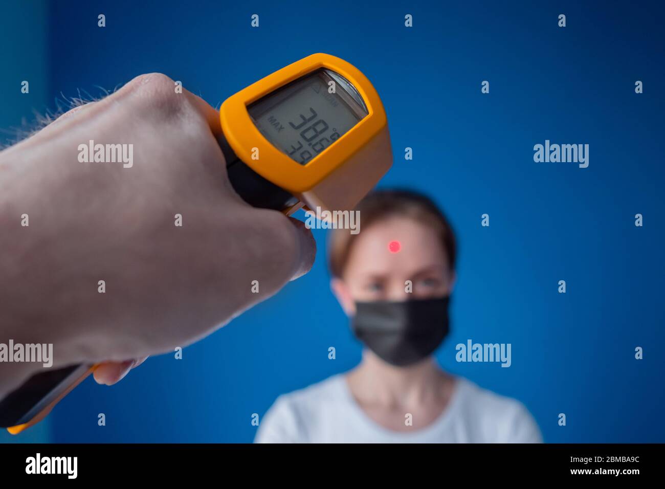 Man hand holding yellow pyrometer and measuring temperature of woman in ...