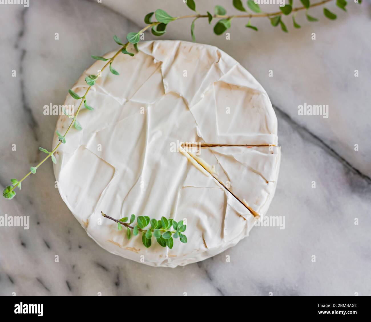 Round Brie cheese with a section cut out on a marble tray on white ...