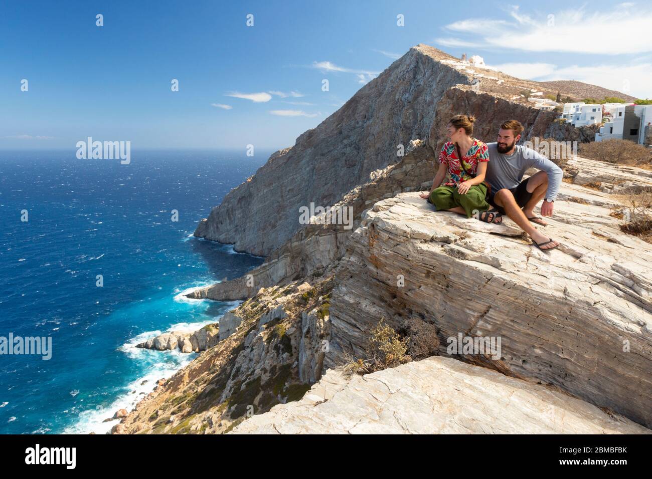 A young couple sitting on the edge of a cliff and enjoying a coastal ...